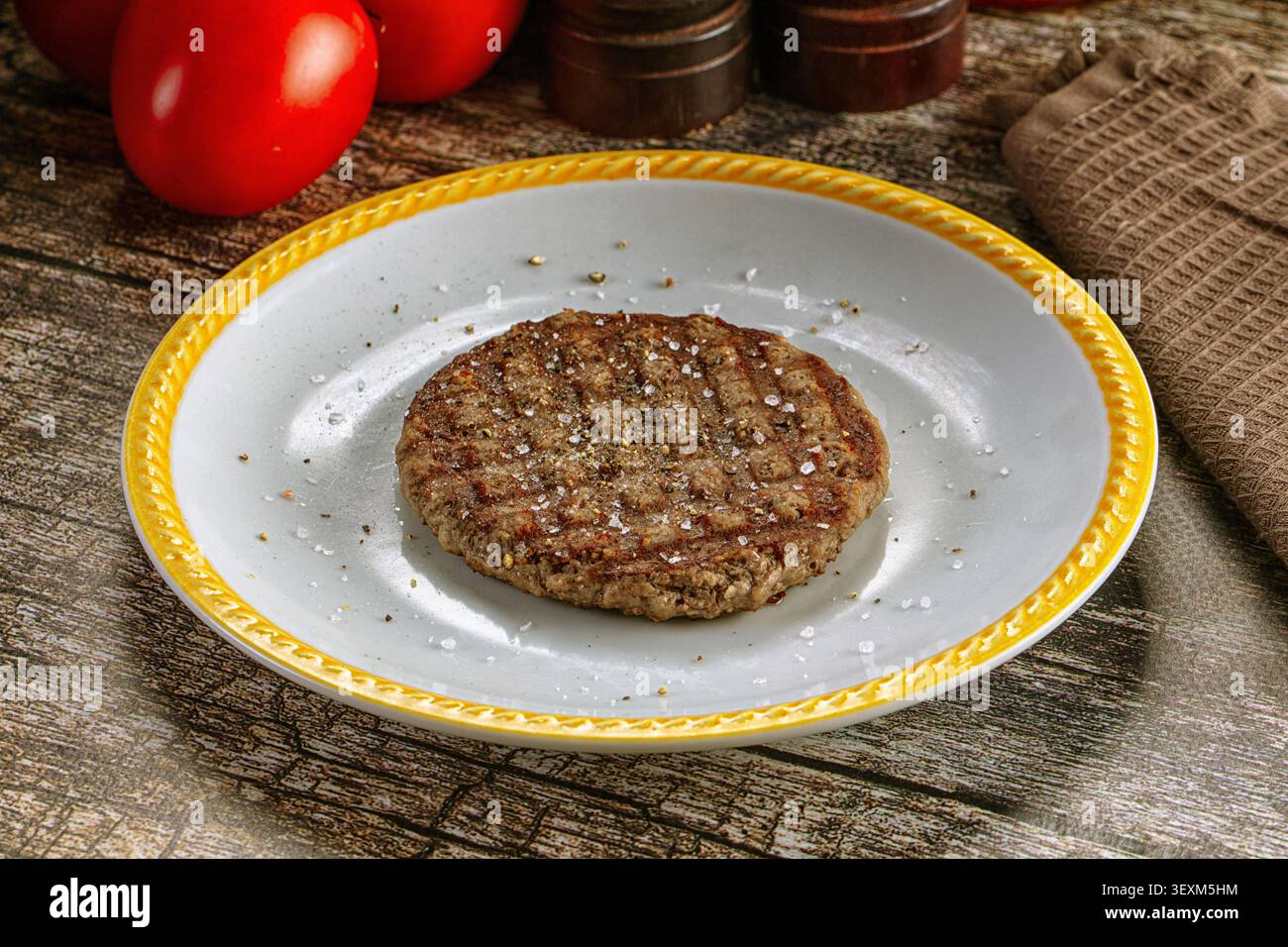 Grilled beef patty centered on white plate with yellow rim, sprinkled ...