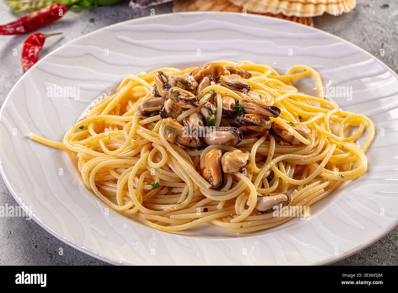 Spaghetti with mussels served on textured white plate. Warm golden ...