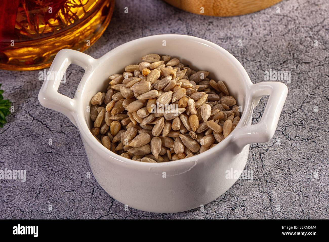 Raw hulled sunflower seeds fill a white ceramic bowl on a gray textured ...