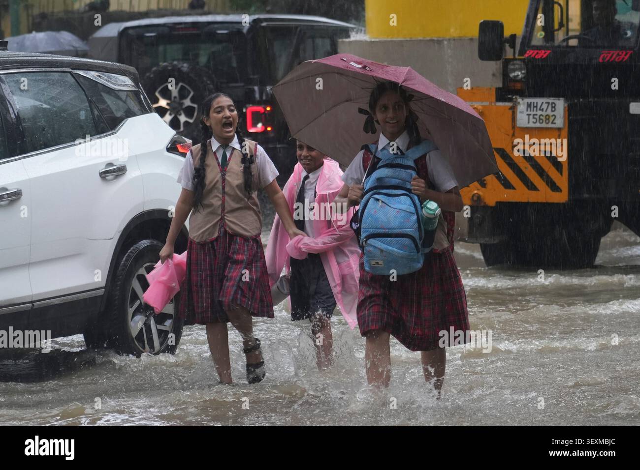 School students walk through a waterlogged street during monsoon rains ...