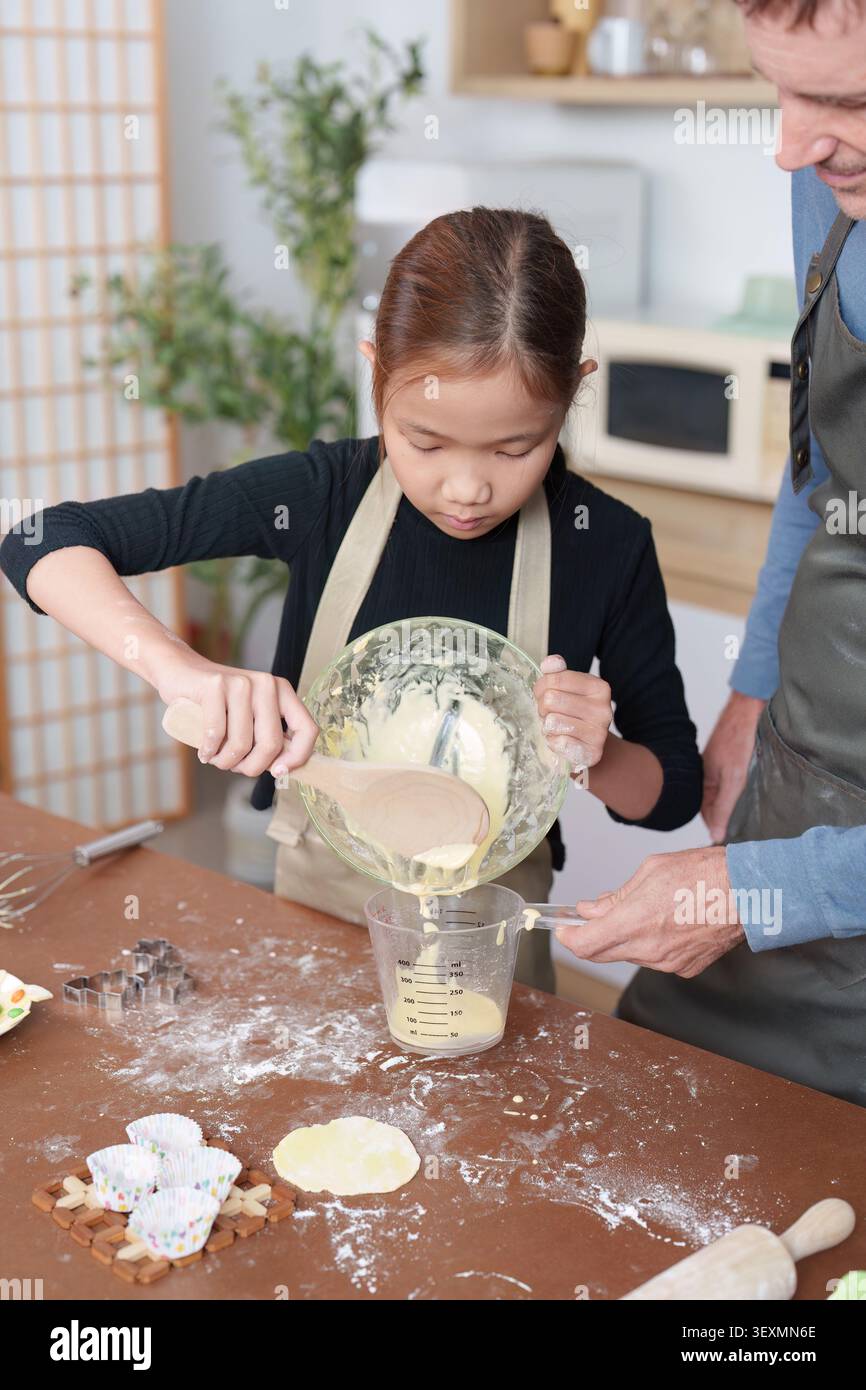 Asian girl pouring cake batter into measuring cup with father in ...
