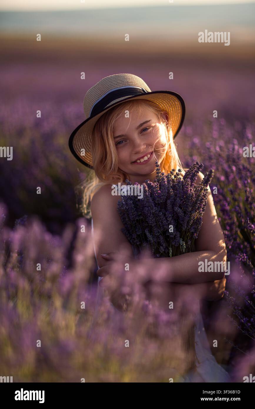 Happy little girl wearing a straw hat stands in a vast purple lavender ...