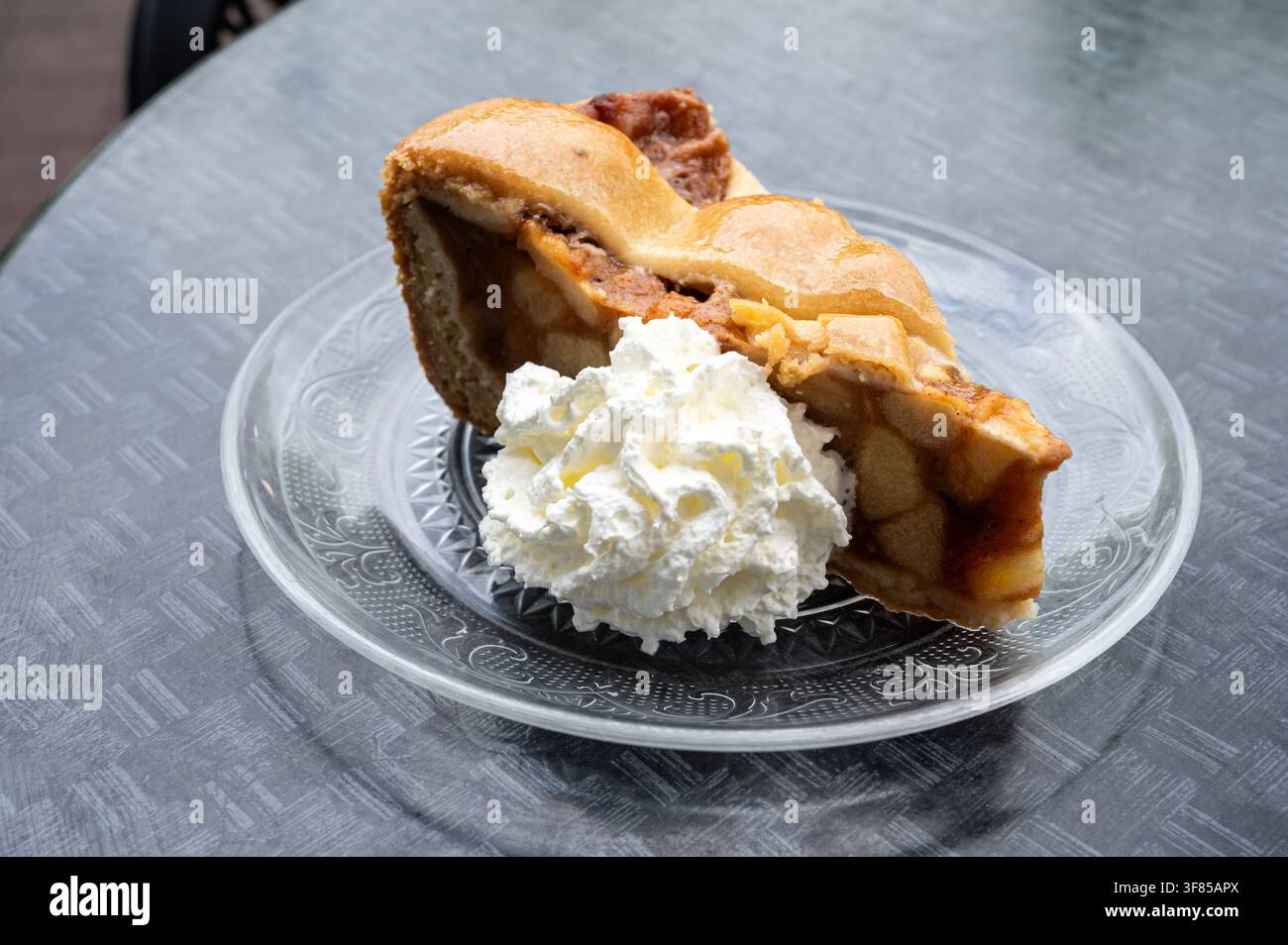 A slice of apple pie served with a dollop of whipped cream on a plate ...