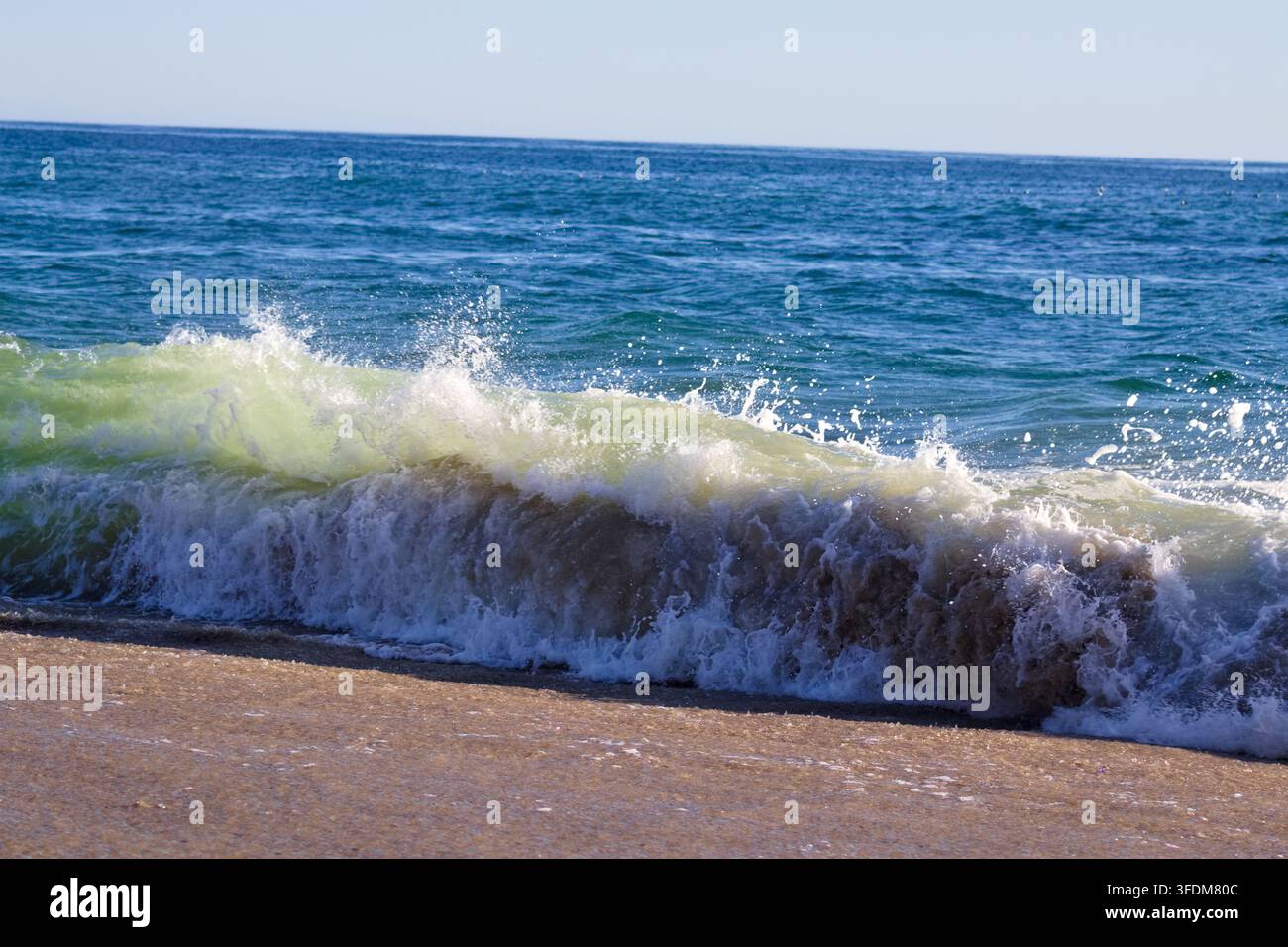 Ocean wave crashes onto sandy beach. Clear blue water meets golden ...