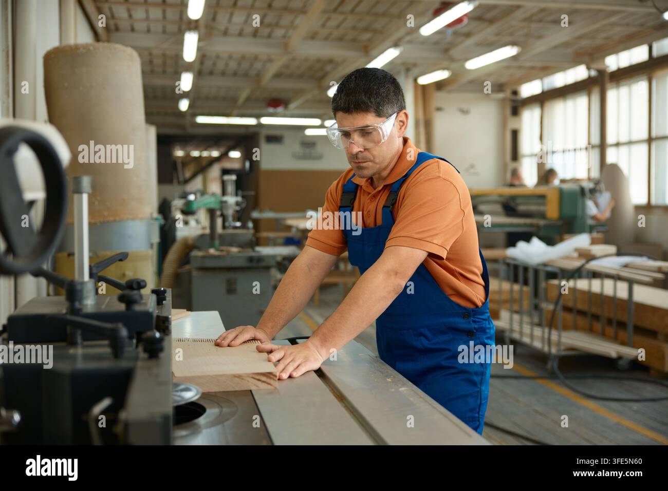 Focused carpenter at table saw pushing plank through blade. Worker ...