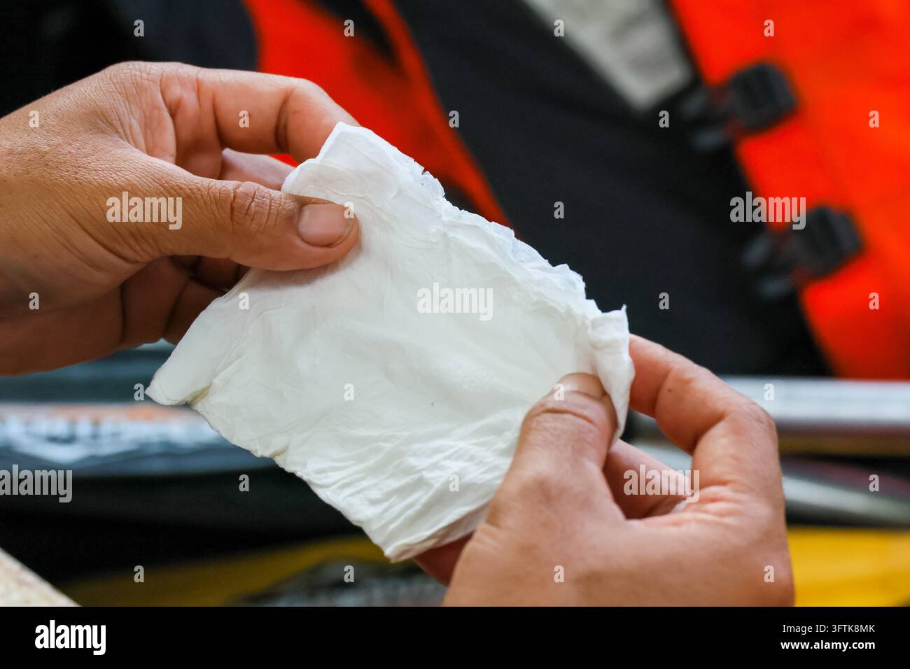 An adult hand holding white tissue paper during outdoor cleanup, with ...