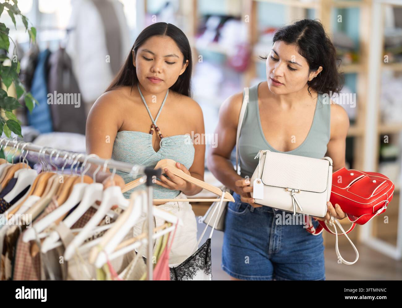 Girl client chooses dress or tank top, female assistant consultant ...