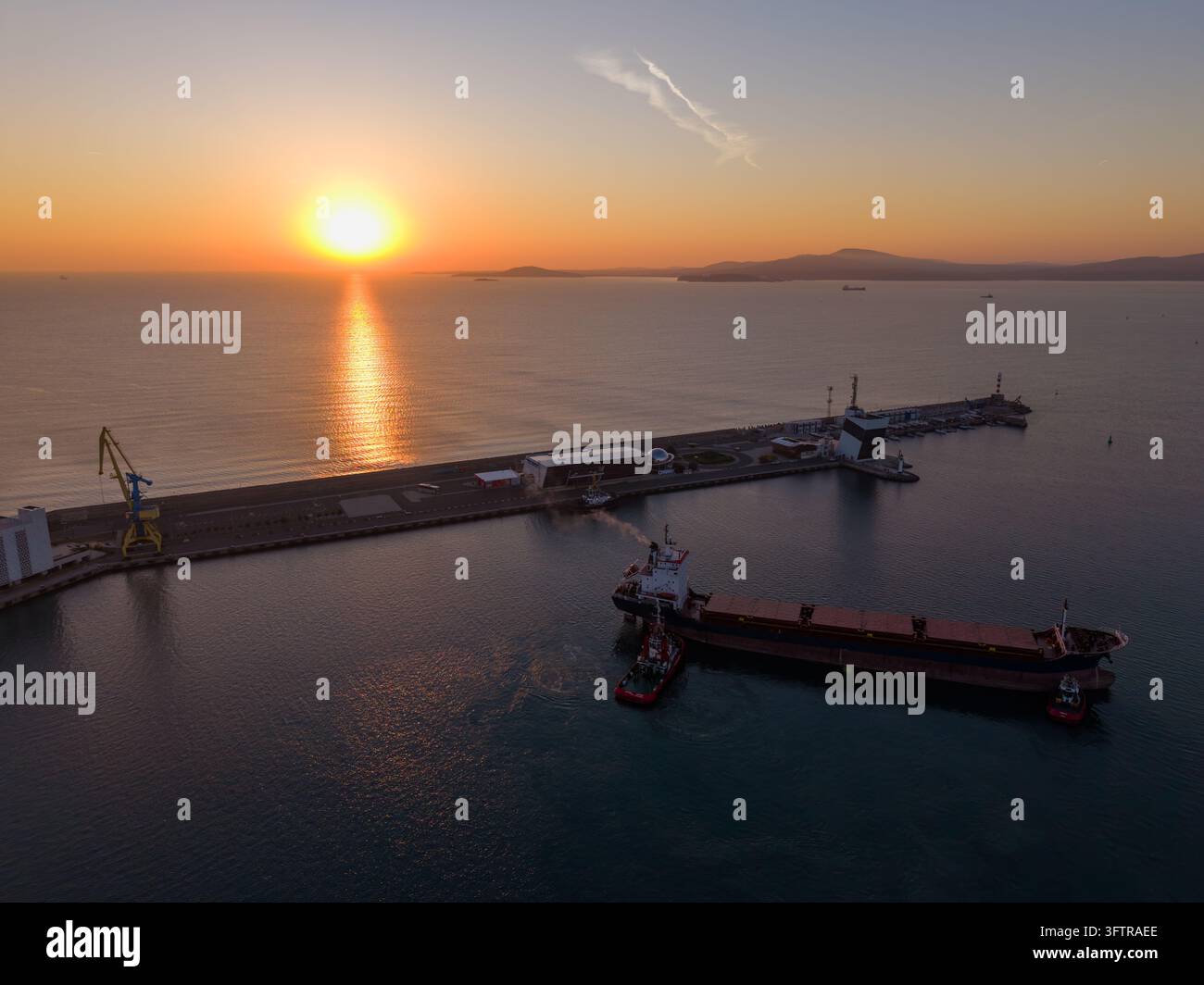 Aerial view of a cargo ship being maneuvered by tugboats in the Port of ...