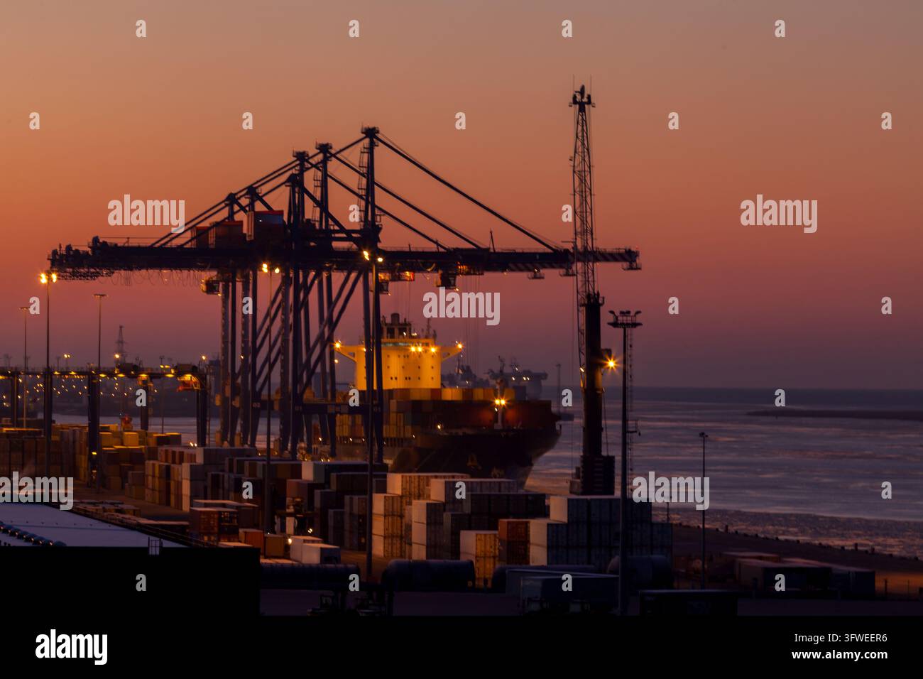 Container cranes and cargo ship at a busy seaport during sunset, with ...