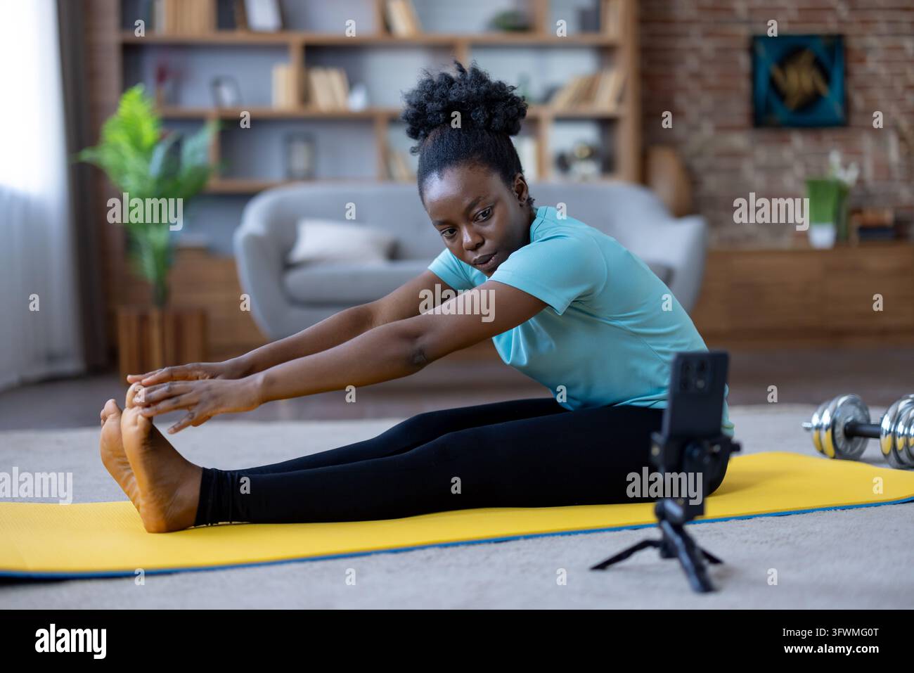 Young woman performs seated hamstring stretch on yoga mat in living ...