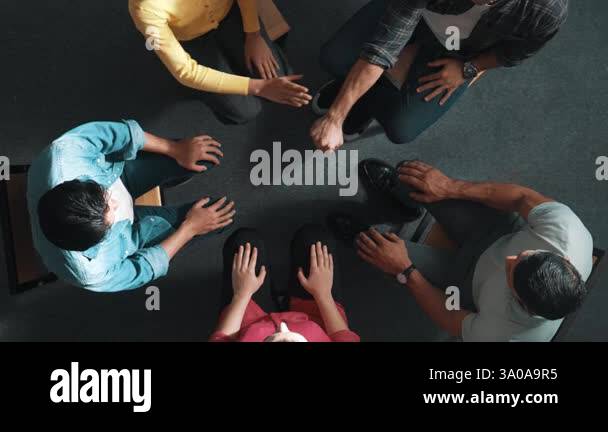 Top down aerial view of diverse business people hold wrist while sitting circle together ...
