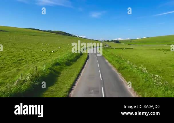 English countryside road stretches through vibrant green hills under a ...