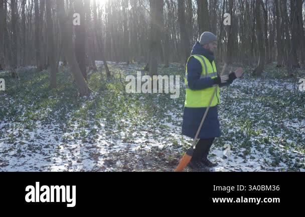 A person wearing a safety vest digs in a snowy forest landscape ...