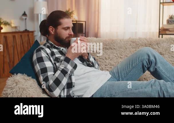 Young man resting lying at home, holding warm cup of coffee or tea with ...