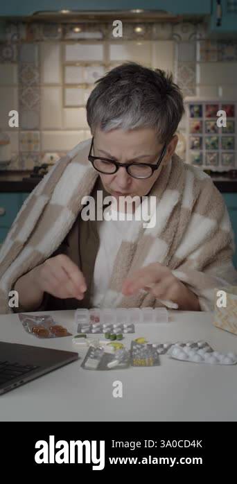 A sick mature woman carefully places pills into a daily drug organizer ...