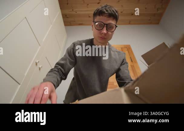 A young man anxiously unpacks clothes from a cardboard box, pulling out ...