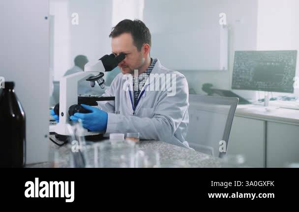 Young male lab technician in white coat looking at samples and using ...