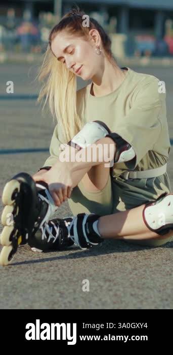 A cheerful woman sits on the ground, tying her roller skates with ...