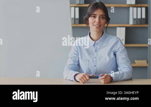 A young woman engages in online education, tutoring students remotely. She sits at a desk, ready ...
