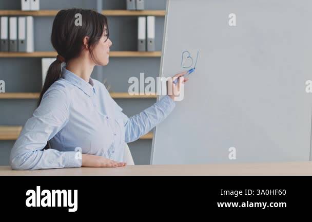 A young woman teaches an online lesson from her home, writing on a ...