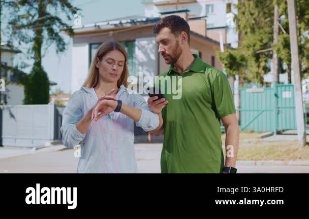 A man and a woman are checking their fitness tracking devices while ...