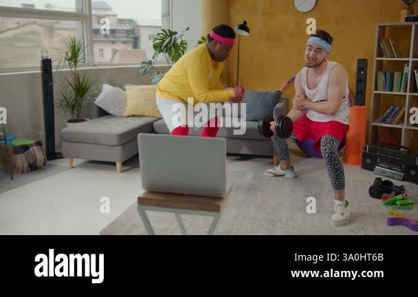 Two men work out in a cozy living room using a laptop for guidance ...