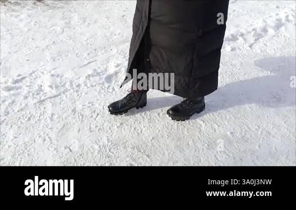 A woman's feet in black boots and a long jacket walk through the snow ...