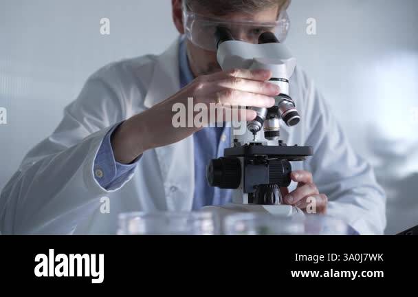 Male scientist wearing lab coat and protective glasses using microscope ...