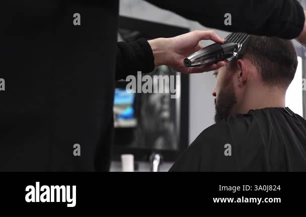 Professional barber skillfully cutting hair of male client with an ...