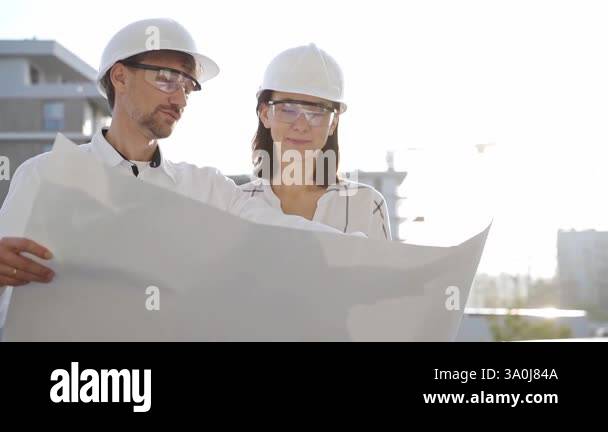 Two architects, wearing safety helmets and glasses, are examining ...