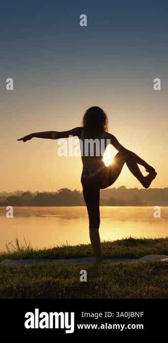A serene silhouette of a yogi in a meditative pose by the waters edge ...