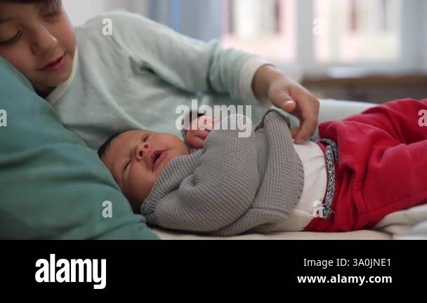 Older sibling lovingly watches over baby on a bed, gently holding baby ...