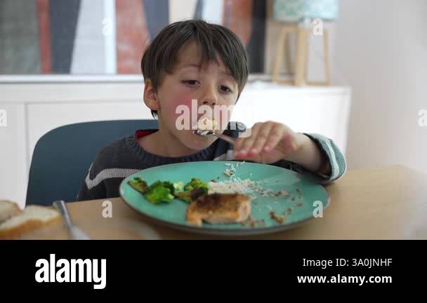 boy eating lunch at home, enthusiastically using a fork, capturing the ...