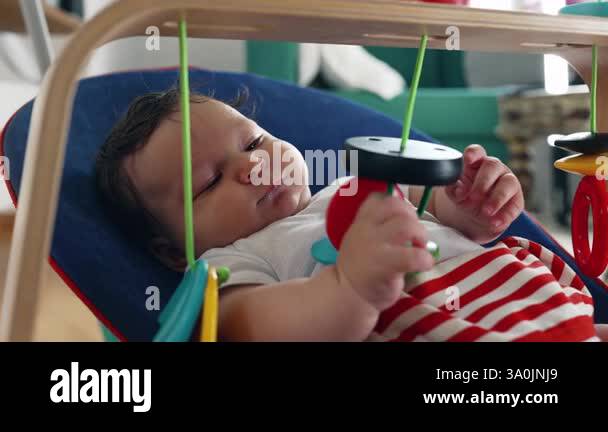Baby lying in a bouncer, reaching out and touching hanging toys ...