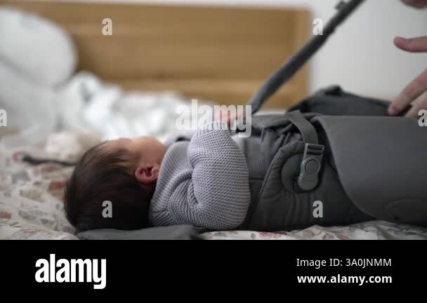 Mother adjusting baby carrier straps, securing newborn in gray knit ...