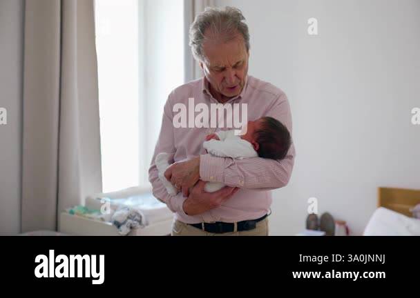 Grandfather holding his newborn grandchild in a brightly lit room ...