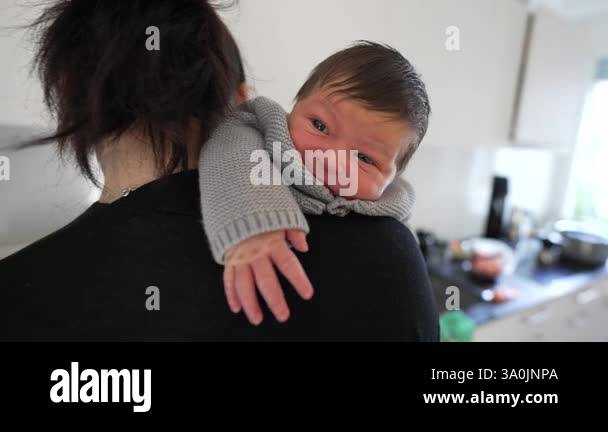 Baby with expressive face looks over mother's shoulder, close-up shot ...