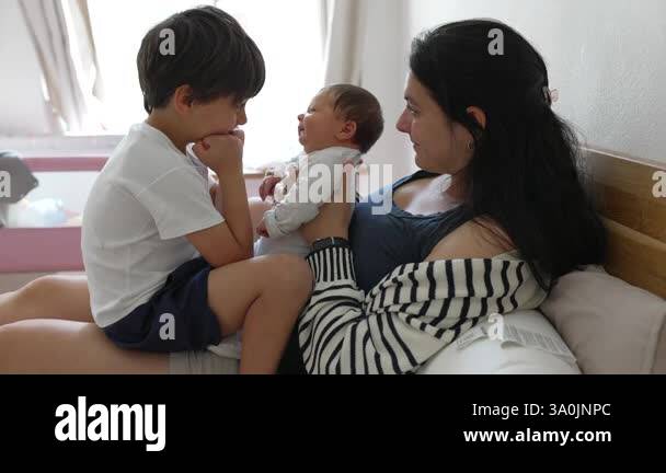 Mother with young son and baby sitting on bed, family interaction ...