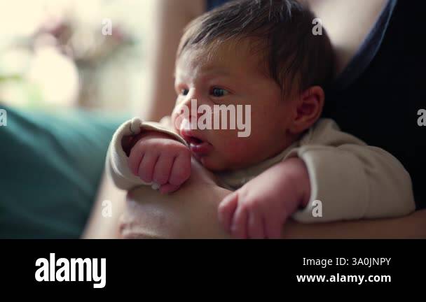 Newborn baby smiles while being held close by parent, capturing a ...