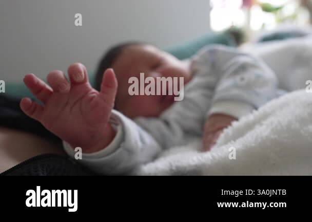 Close-up of a newborn baby stretching out its tiny hand while resting ...