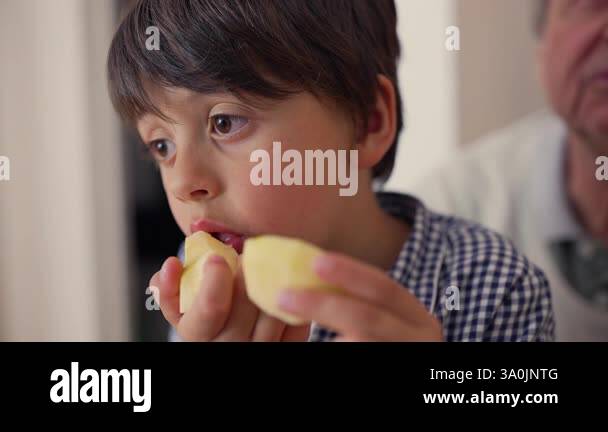 Young boy eating apple slice, close-up on face, thoughtful expression ...
