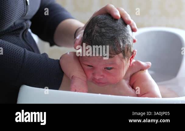 Mother carefully washing her newborn baby's hair during bath time ...