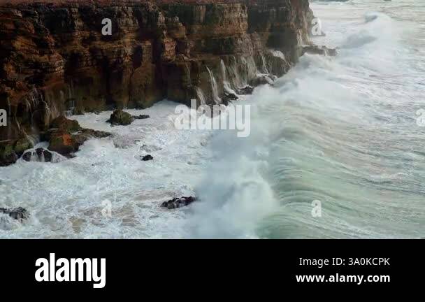 Towering ocean waves crash against jagged cliffs, creating a dramatic ...