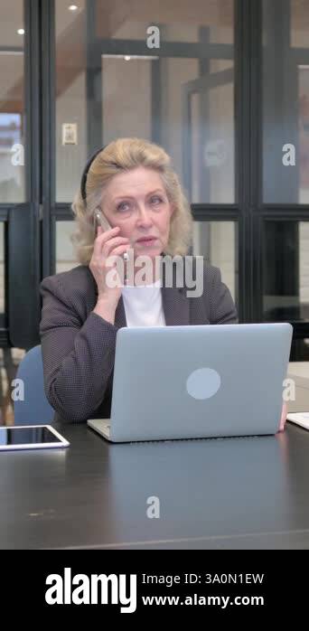 Senior Old Business Woman Talking on Phone while Working on Laptop at ...