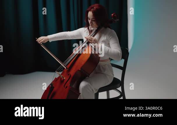 A beautiful woman sitting and playing the cello in a studio on a white ...