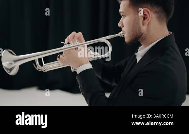 A young man dressed in a suit plays the trumpet with desire and ...
