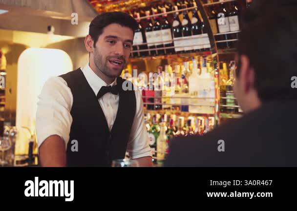 Focusing on smiling smart bartender preparing drinks at luxurious bar while engaging lively ...