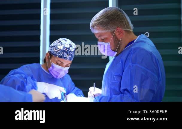 Attentive female surgeon carefully uses electric scissors. Bearded ...