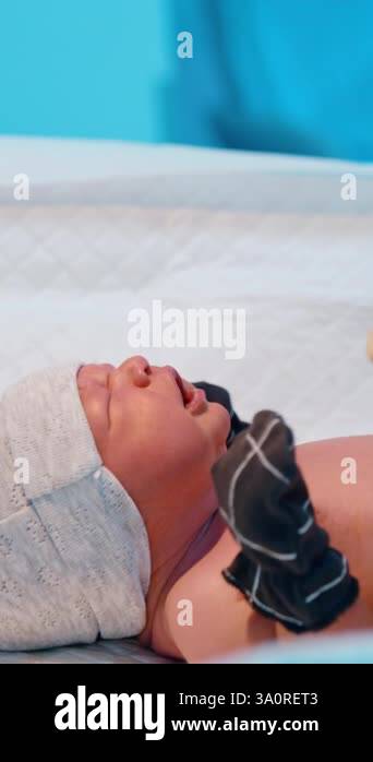 Just born infant crying bitterly on the table. Newborn baby is dressed ...