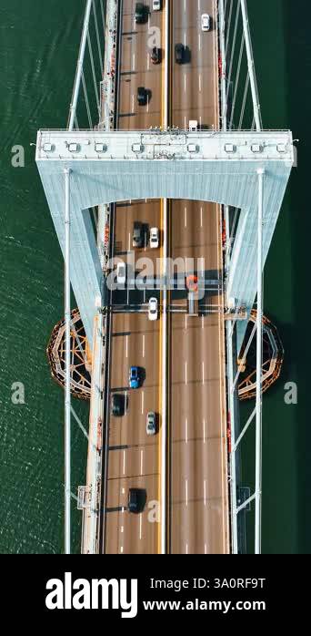 Part of the suspension bridge over sea-green water. Cars move by the ...